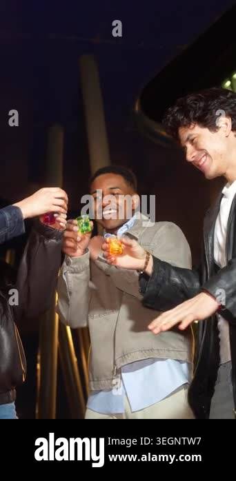 Joyful multiethnic friends toasting and drinking colorful alcohol shots ...