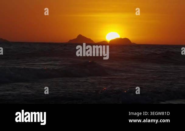 Dramatic sunset over water with waves, people in silhouette on beach ...