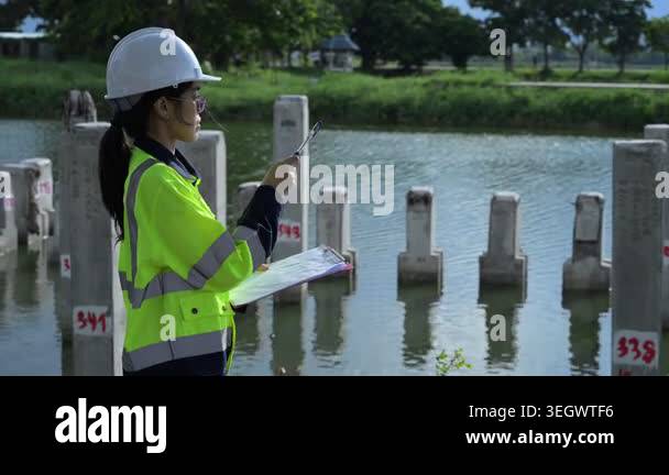Female engineer in safety gear inspecting water level markers near a ...