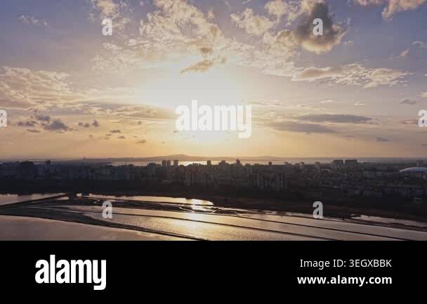 The sun sets behind a city skyline, casting long shadows. A river ...