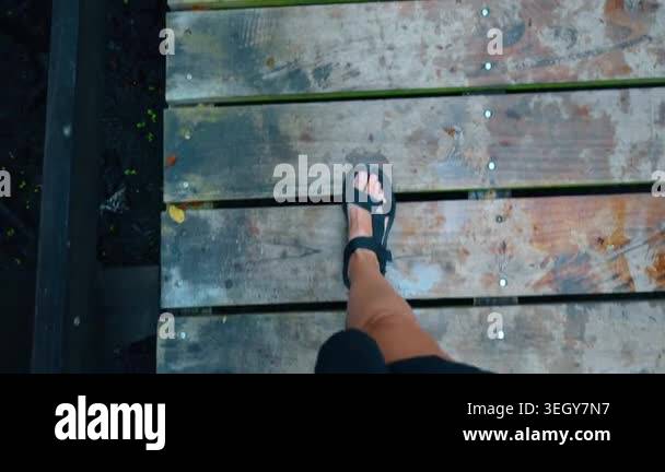Female feet walk by the wooden pier. Woman steps over the large black ...