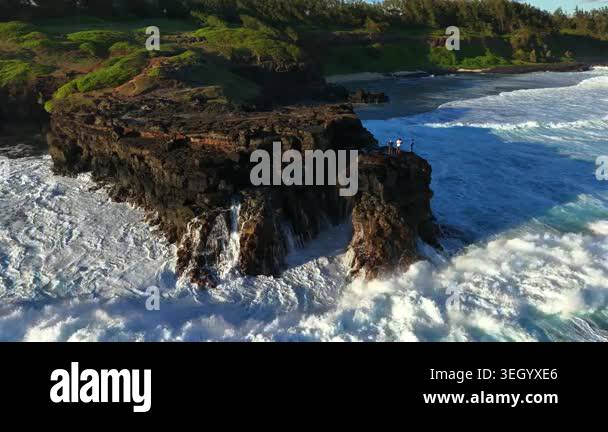 Rocky coastline with crashing waves under a clear blue sky and lush ...