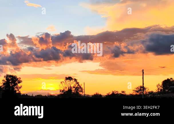 Golden sunset sky with dramatic orange clouds over dark silhouette ...