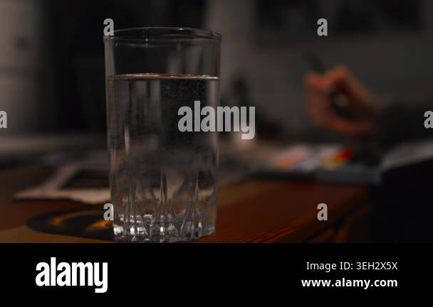 Glass Of Water On Wooden Table With Blurred Hand Reaching In Background ...