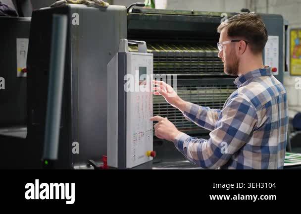 Young industrial worker with safety glasses programming a modern offset ...
