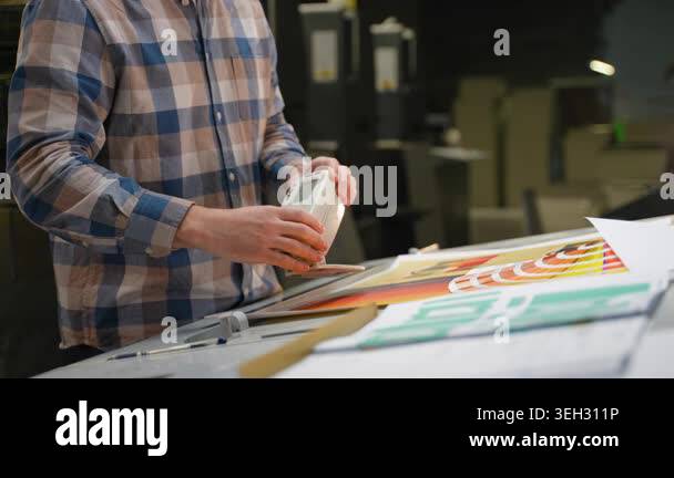 Male worker in a print plant checking the color quality of a poster ...