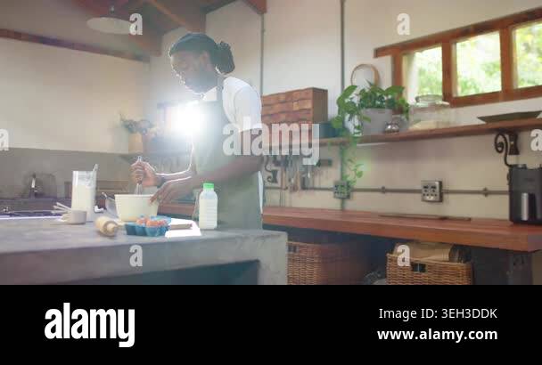 African American man in green apron whisking batter at island, sun ...