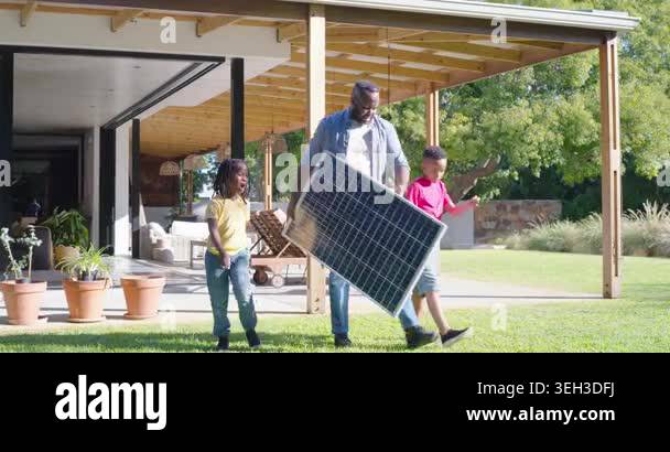 African American family dad carrying solar panel from patio to lawn as ...