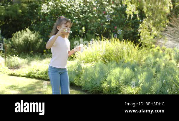 African child dipping wand into bottle, blowing, stepping to chase ...