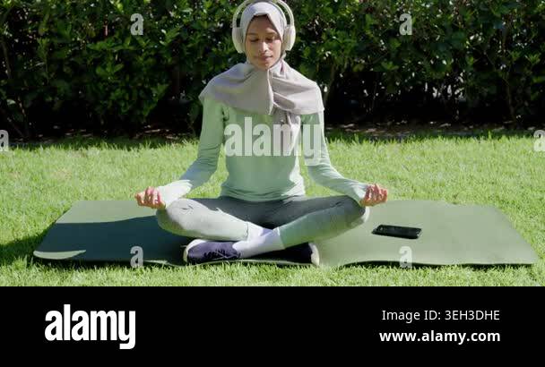 Adult African American woman meditating on mat in yard hijab cell ...