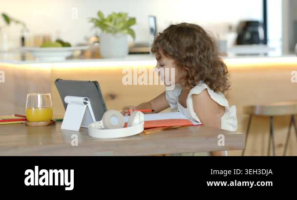 Parents noticing preschool girl using tablet at kitchen table, leaning ...