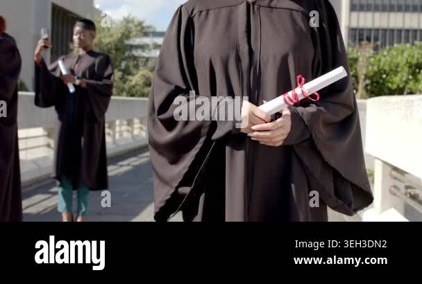Ceremony start Hispanic female gowned grad walking onto terrace holding ...