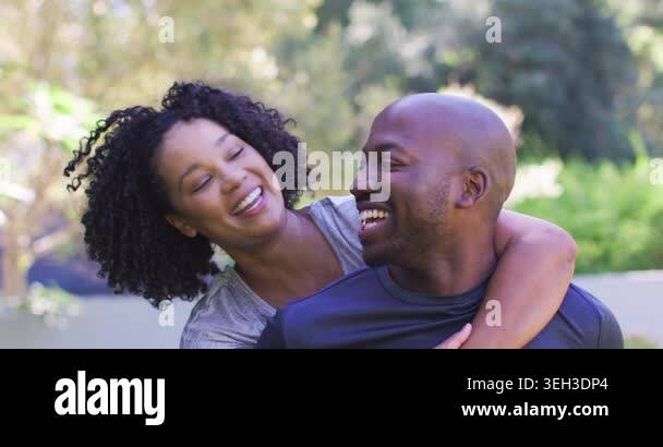 African American couple playfully laughing, piggybacking in yard by low ...