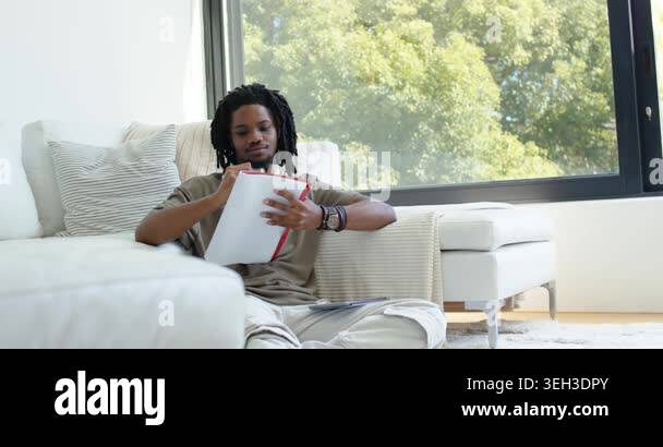 African American man sitting on rug in living room paging white ...