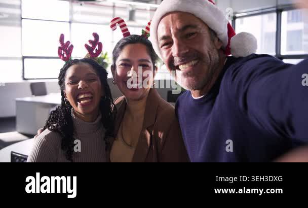 Diverse coworkers taking festive selfie while adjusting antlers and ...