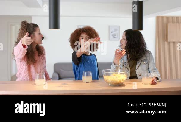 Diverse female friends starting chat, gesturing toward chips at home ...