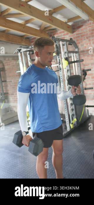 Vertical video: Man starting right-arm biceps curls in garage holding ...
