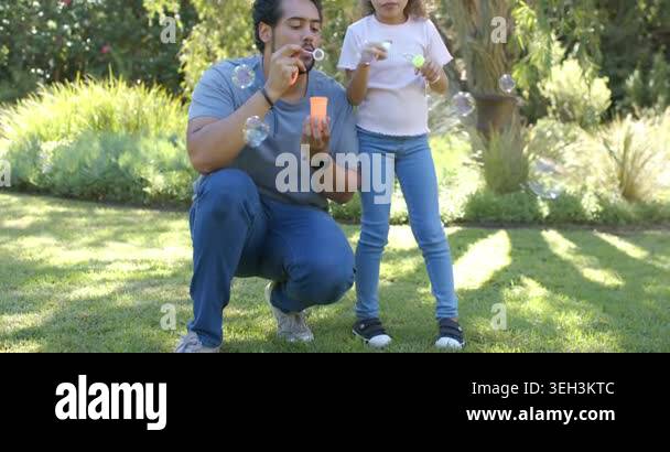 African American man and girl playing on lawn man blowing bubbles from ...