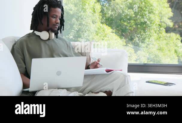 African American man prompted by laptop, checking and writing in red ...