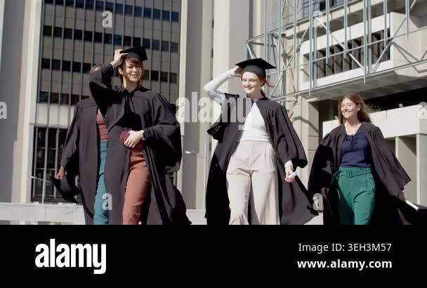 Diverse female graduates walking in plaza adjusting caps with ...