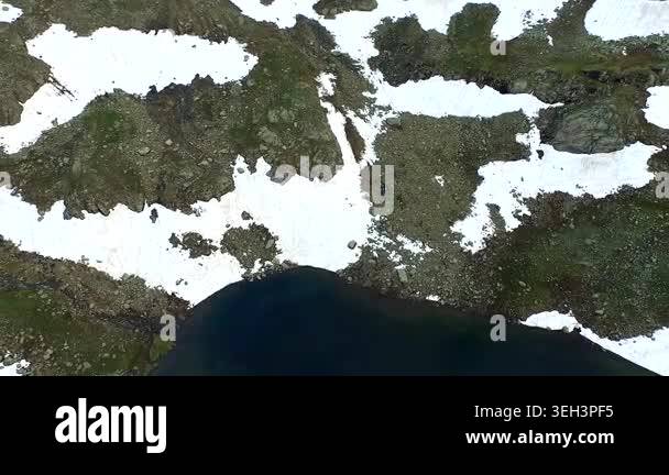 Aerial view of alpine mountain lake surrounded by melting spring snow ...