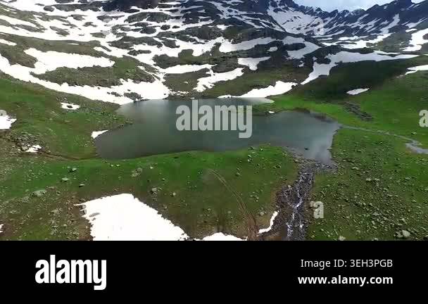 Aerial view of alpine mountain lake surrounded by melting spring snow ...