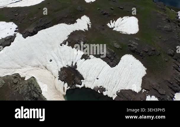 Aerial view of alpine mountain lake surrounded by melting spring snow ...