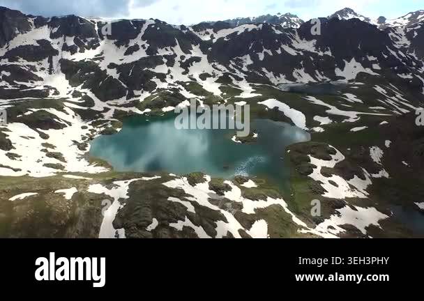Aerial view of alpine mountain lake surrounded by melting spring snow ...