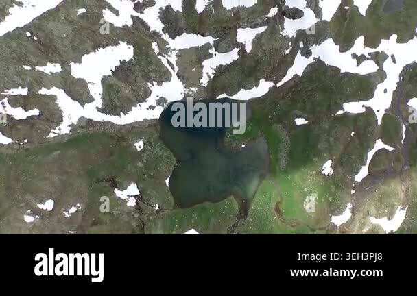 Aerial view of alpine mountain lake surrounded by melting spring snow ...
