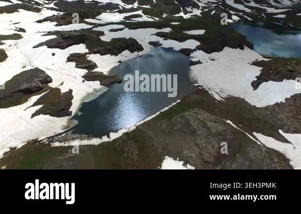 Aerial view of alpine mountain lake surrounded by melting spring snow ...