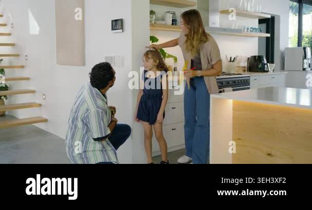Diverse family measuring daughter in kitchen, dad with yellow tape, mom ...