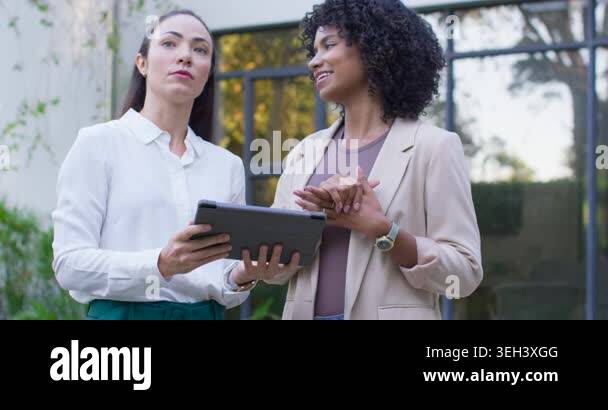 Diverse female coworkers in work attire reviewing tablet report for ...