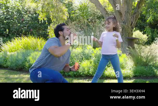 African American dad guiding child blowing and popping bubbles on lawn ...