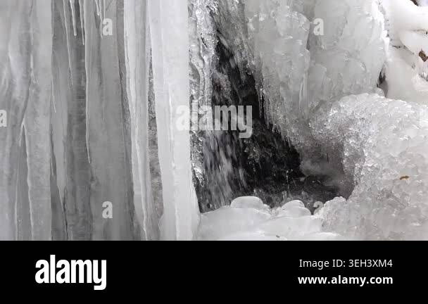 Many crowded icicles cover a natural frozen waterfall in cold air in ...