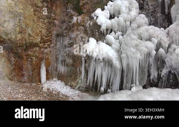 Many crowded icicles cover a natural frozen waterfall in cold air in ...