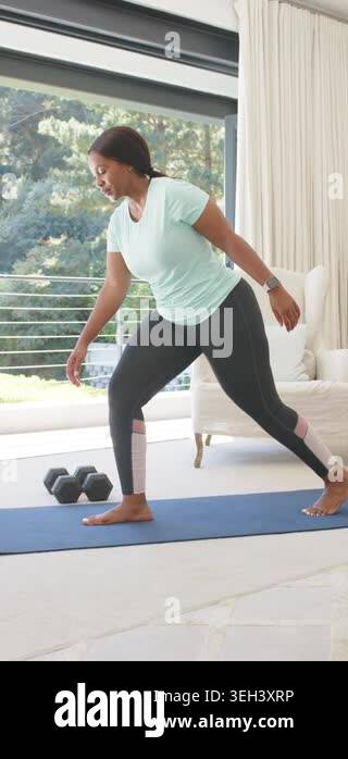 Vertical video: African woman stepping into twist lunge on mat at home ...
