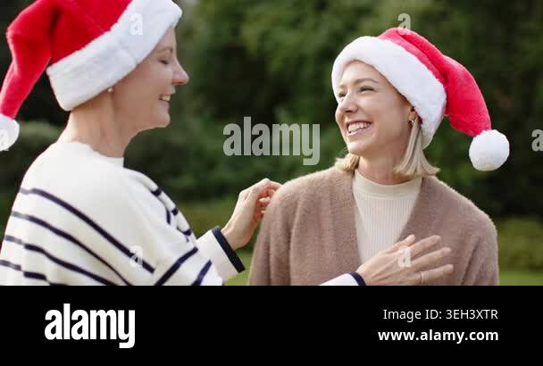 Mother and daughter in Santa hats touching shoulders pointing at trees ...