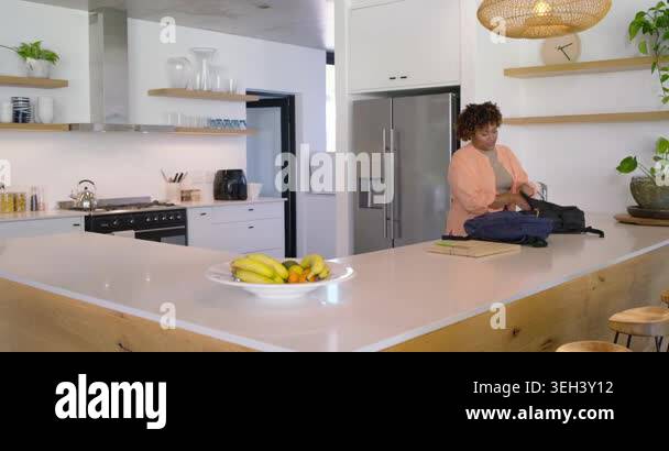 African American woman unpacking backpack in kitchen, scanning room ...