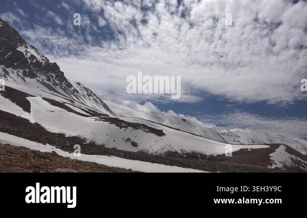 Timelapse clouds drift over snow patched mountain slopes along the ...