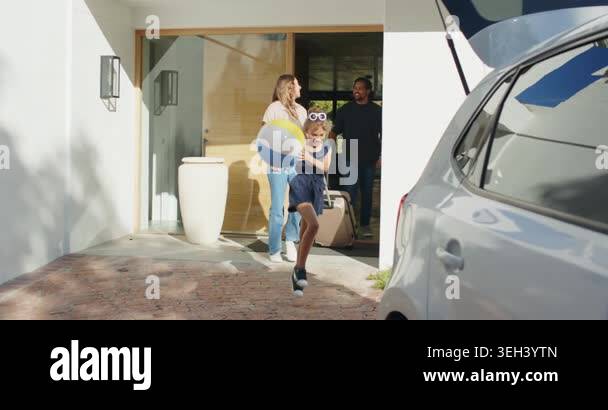 Diverse family child running from doorway on driveway bouncing ball ...