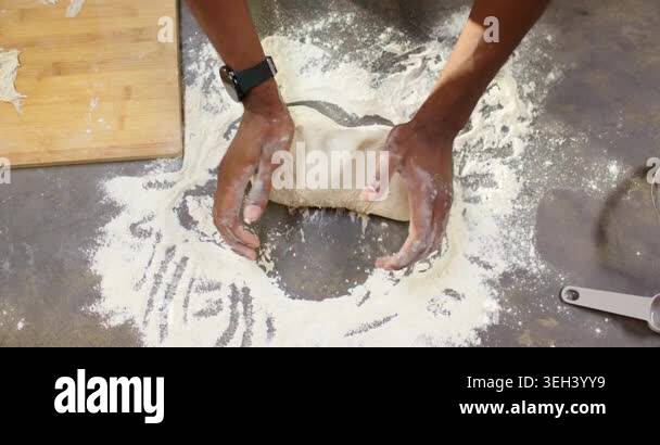 Floured hands are cupping and folding dough on worktop, tucking ...