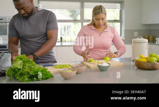 Couple starting salad prep at kitchen island chopping lettuce dicing ...