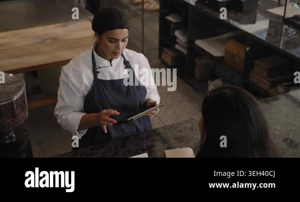 Female baker tapping tablet selecting pastry as customer with phone ...