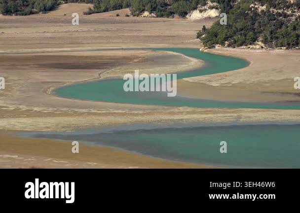 Thin water seepage winding through a drained riverbed across arid plain ...
