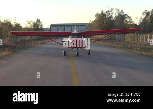 Red single engine airplane taxiing from hangar toward airstrip on quiet ...