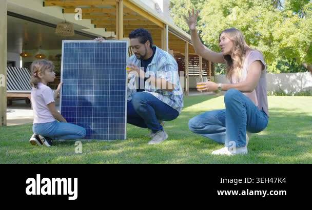 Diverse family placing solar panel upright on lawn, holding juice ...