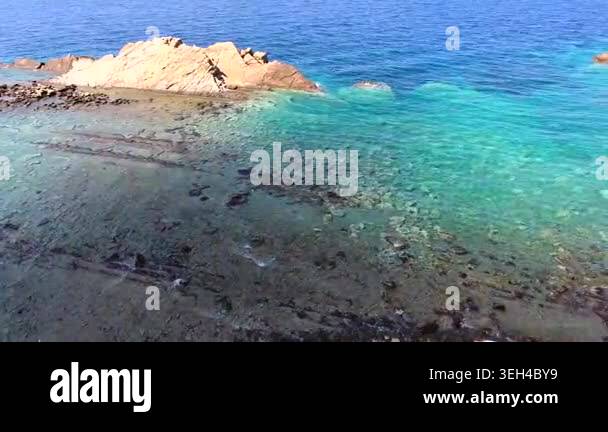 Aerial drone view of tiny rocky islet in clear shallow sea beside ...