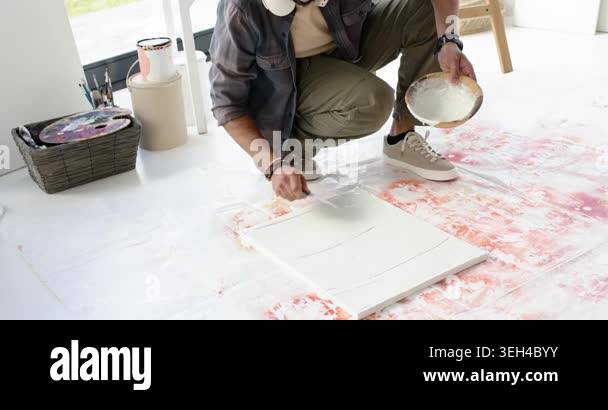 Artist placing canvas on paint-stained tarp, spreading white primer ...