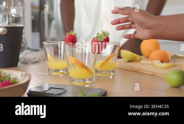 Hands are placing strawberries on glass rims on countertop as blender ...