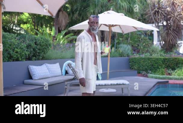 African senior man walking from left on wooden pool deck in lounge set ...